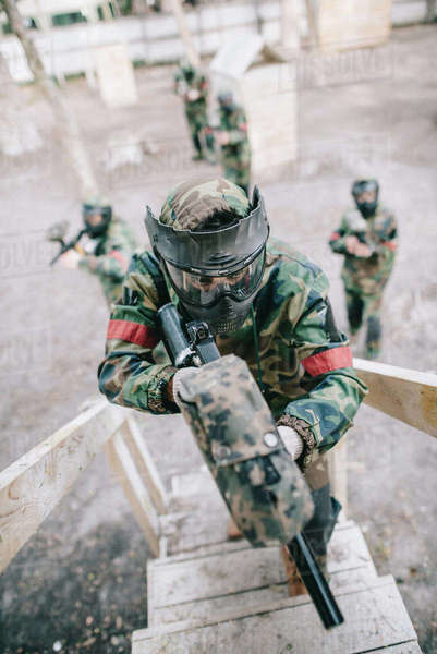 High angle view of paintball player aiming by marker gun and running on ...