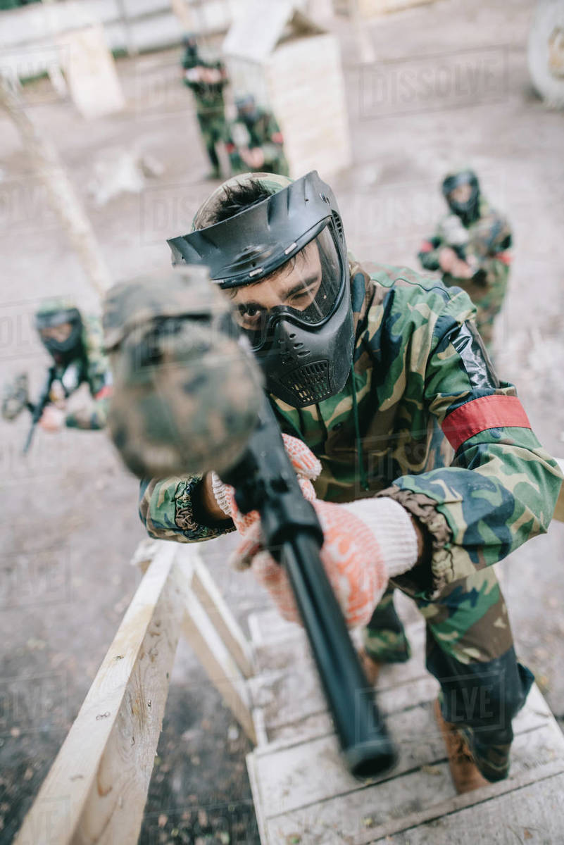 High angle view of male paintball player aiming by marker gun and ...