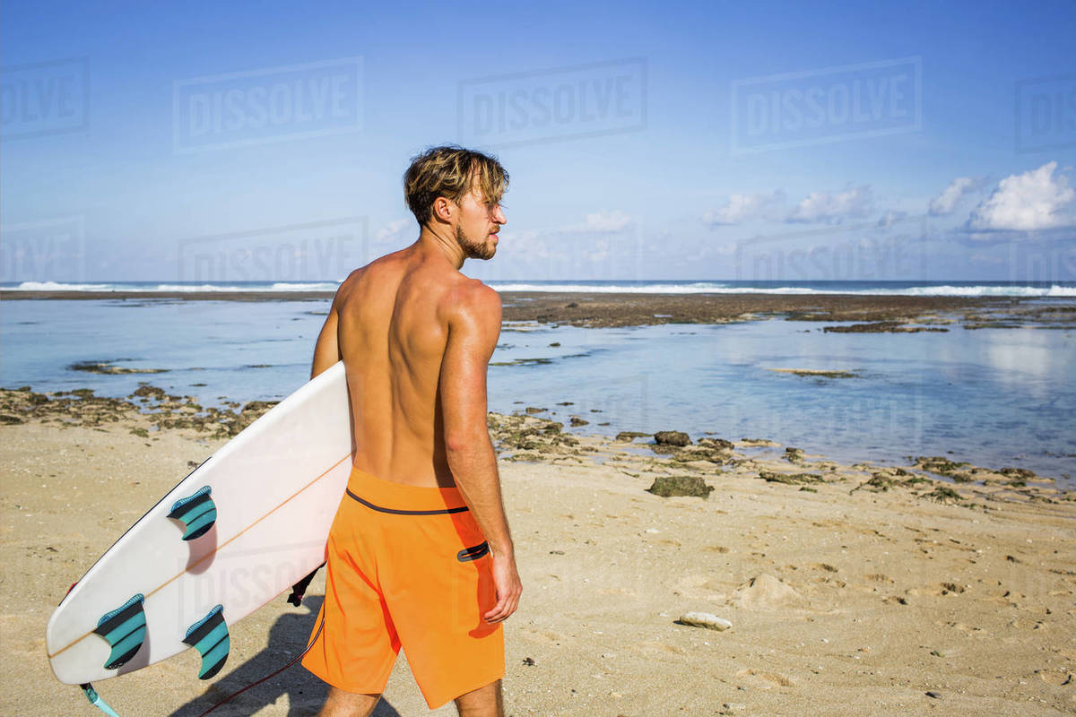 Back view of surfer with surfing board standing on sandy beach on ...