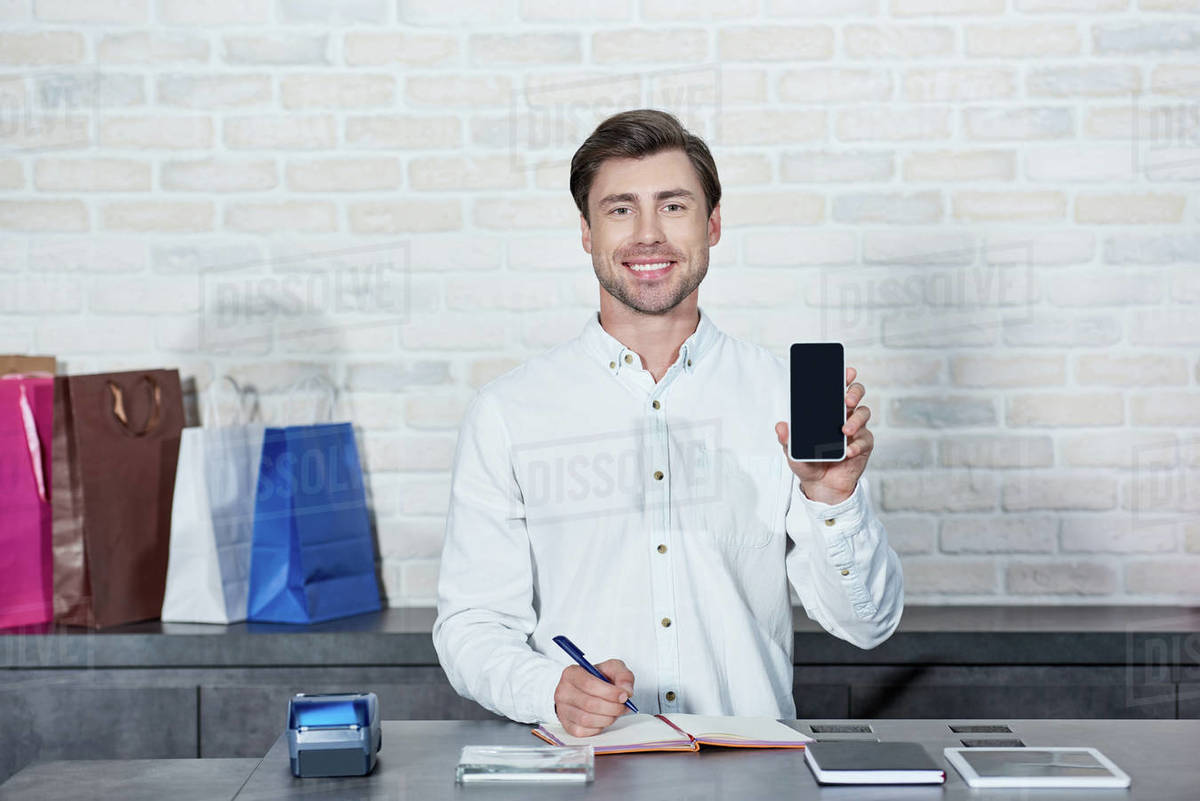 Handsome young salesman holding smartphone with blank screen and ...