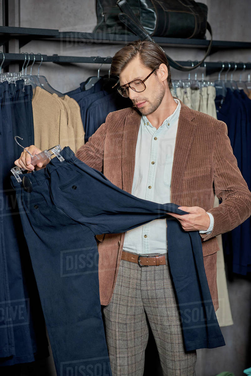 Handsome man in eyeglasses holding hanger with stylish pants in ...