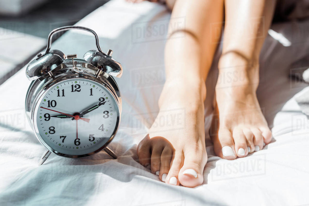 Close-up partial view of female feet and alarm clock on bed - Royalty ...