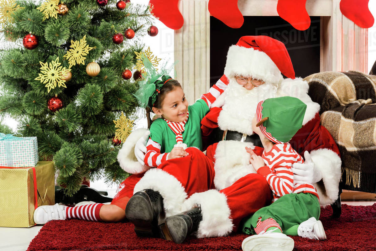 Santa embracing excited kids while they sitting on floor in front of ...