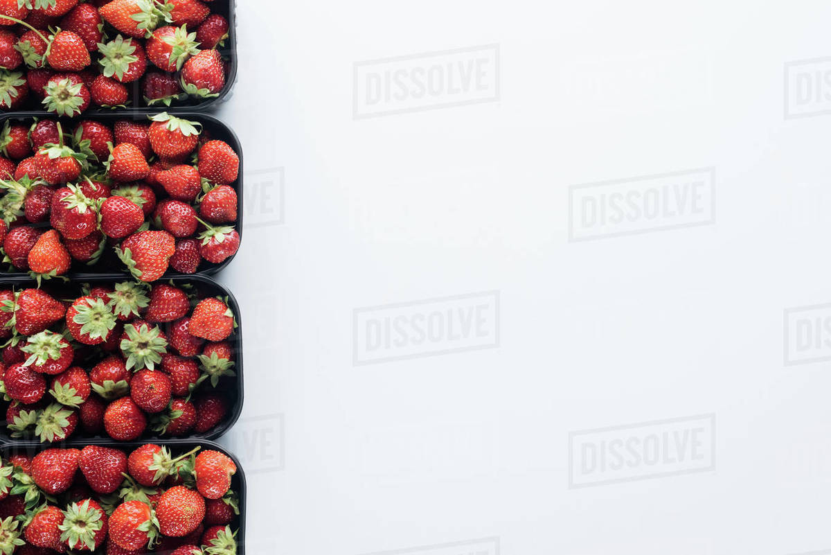 Top view of row of containers with ripe strawberries on white tabletop ...