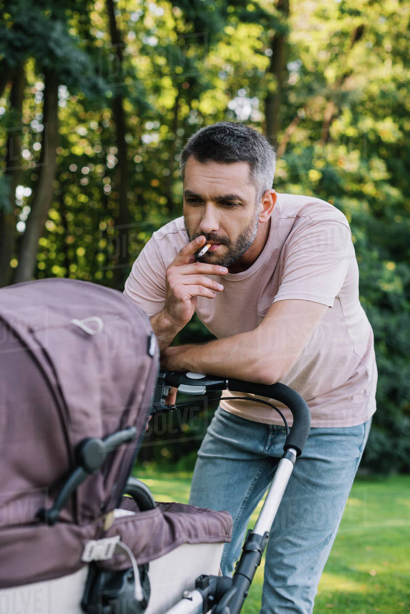 Father smoking cigarette near baby carriage in park - Stock Photo ...