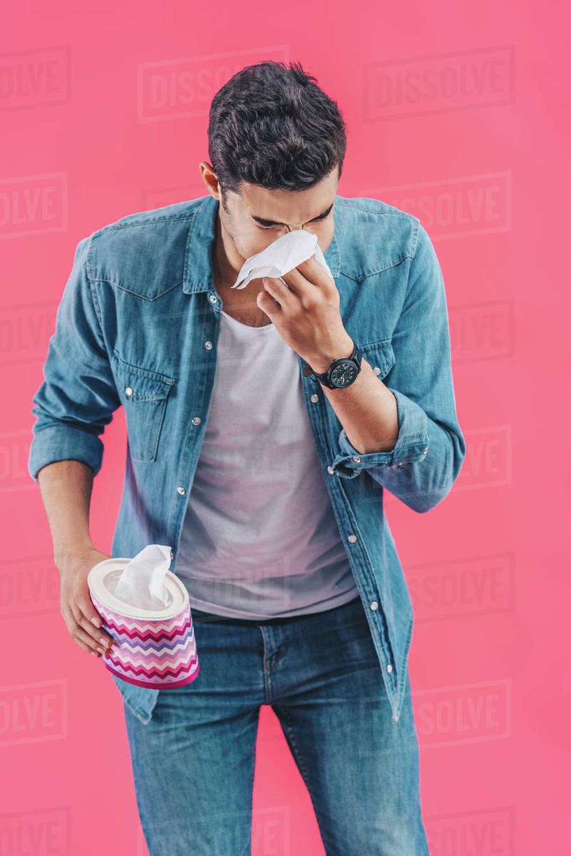 Young man with tissue box crying and wiping nose isolated on pink ...