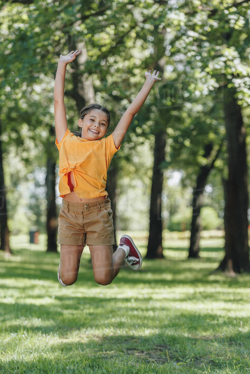 Adorable happy child jumping and smiling at camera in park - Royalty ...