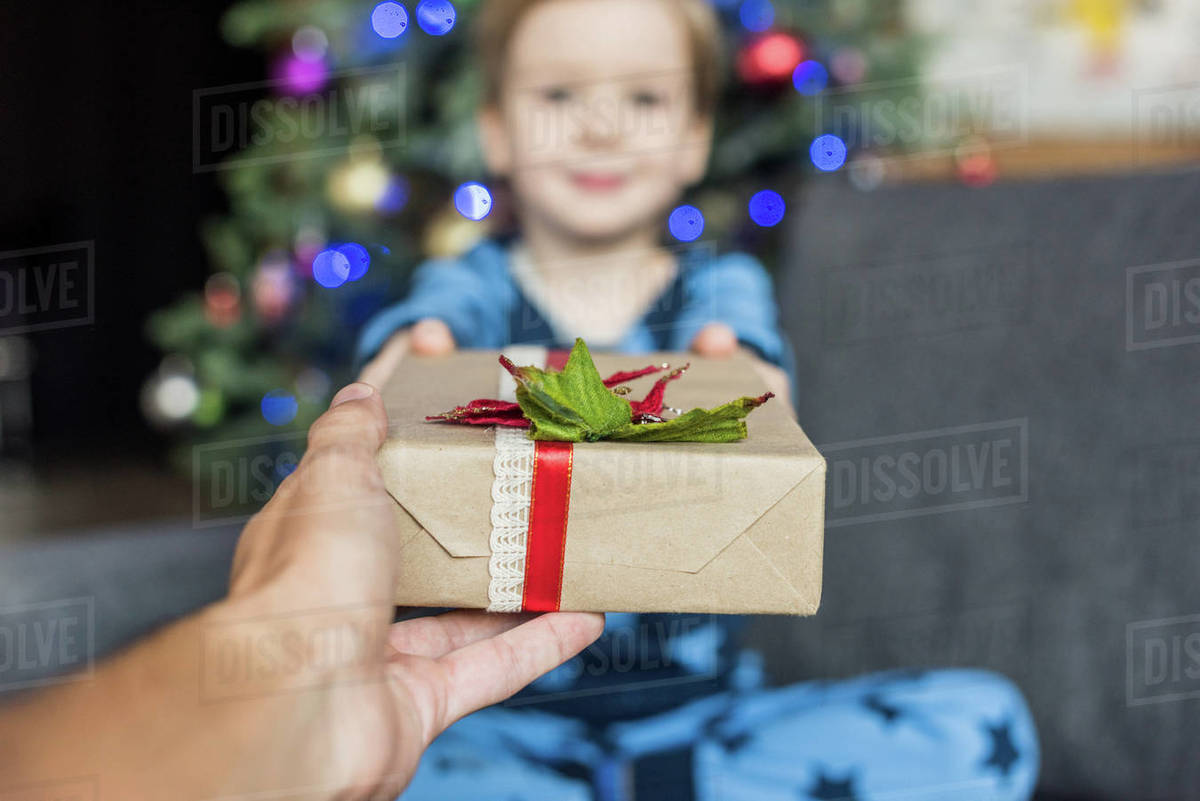 Cropped shot of parent presenting christmas gift to happy little child ...