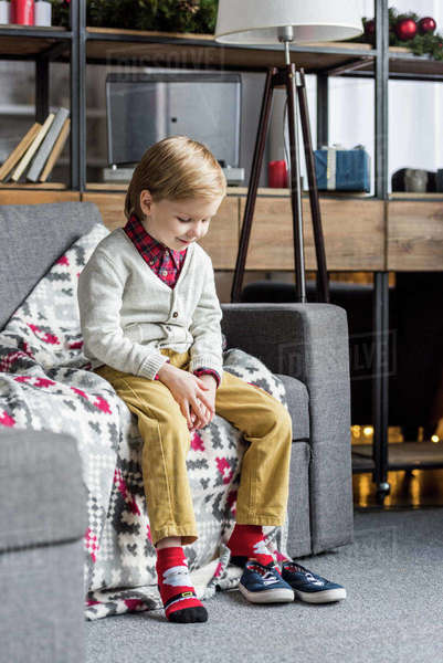 Adorable happy child sitting on sofa and looking at shoes - Stock Photo ...