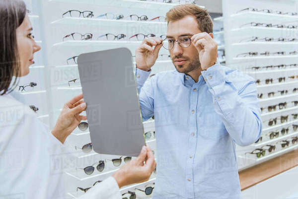 Side view of female optometrist holding mirror while man choosing ...