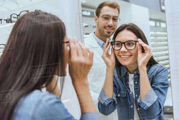 Rear view of cheerful woman choosing eyeglasses and looking at mirror ...