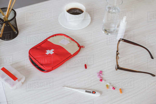 First aid kit, cup of coffee and pills on table in office - Royalty ...