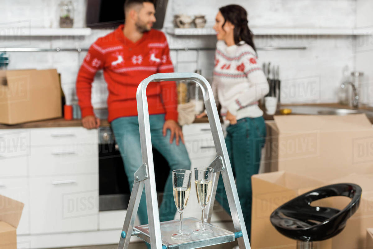 selective focus of champagne glasses on ladder and couple standing ...