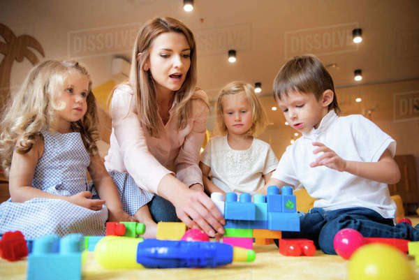 Caucasian educator helping kids playing with constructor in ...