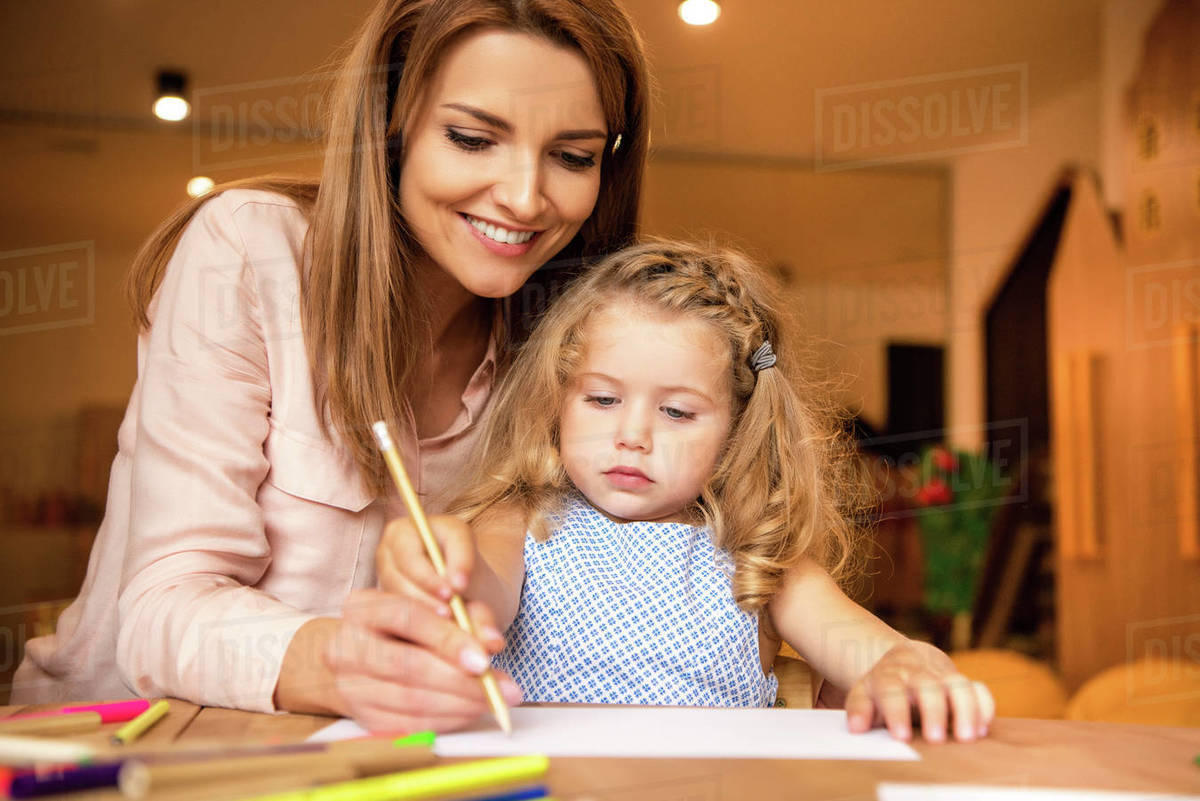 Smiling educator helping kid drawing in kindergarten - Stock Photo ...