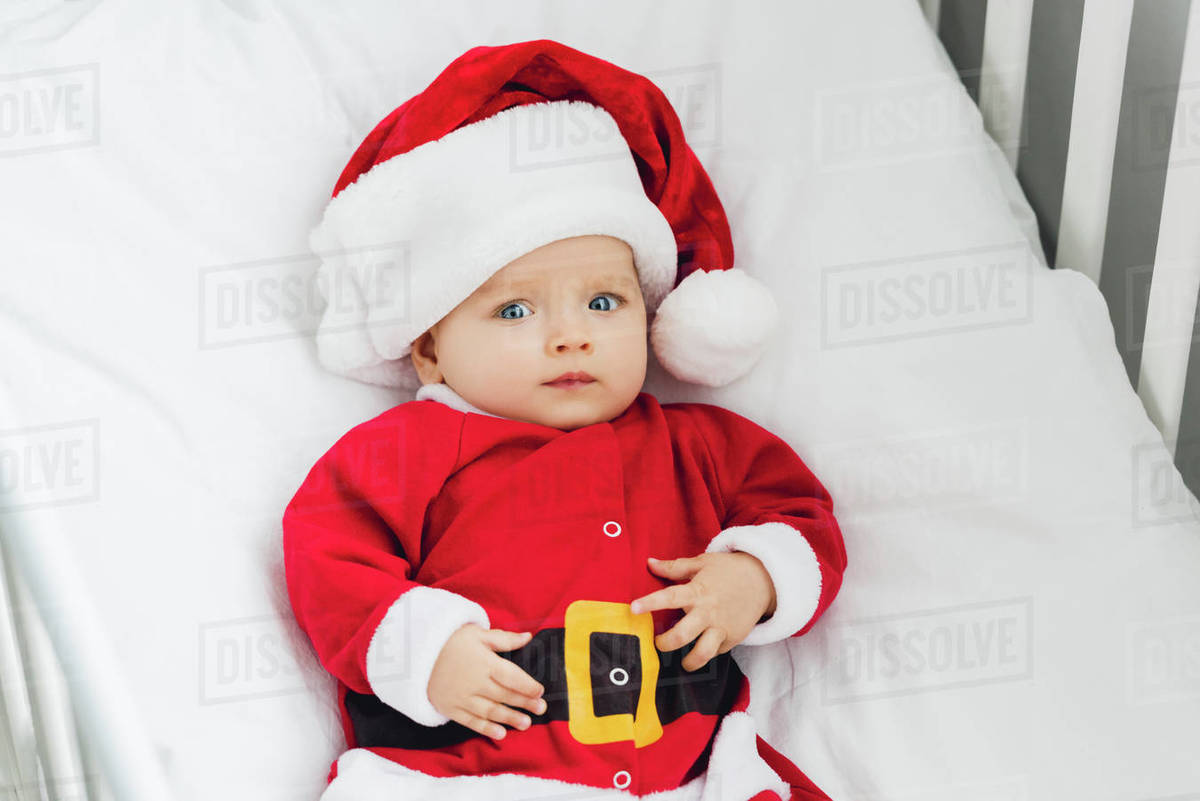 High angle view of adorable little baby in santa suit lying in bed and ...