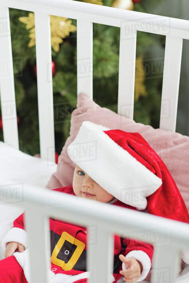 High angle view of adorable little baby in santa suit lying in crib ...