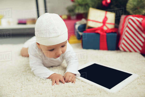 Adorable little baby with tablet lying on floor with christmas gifts ...