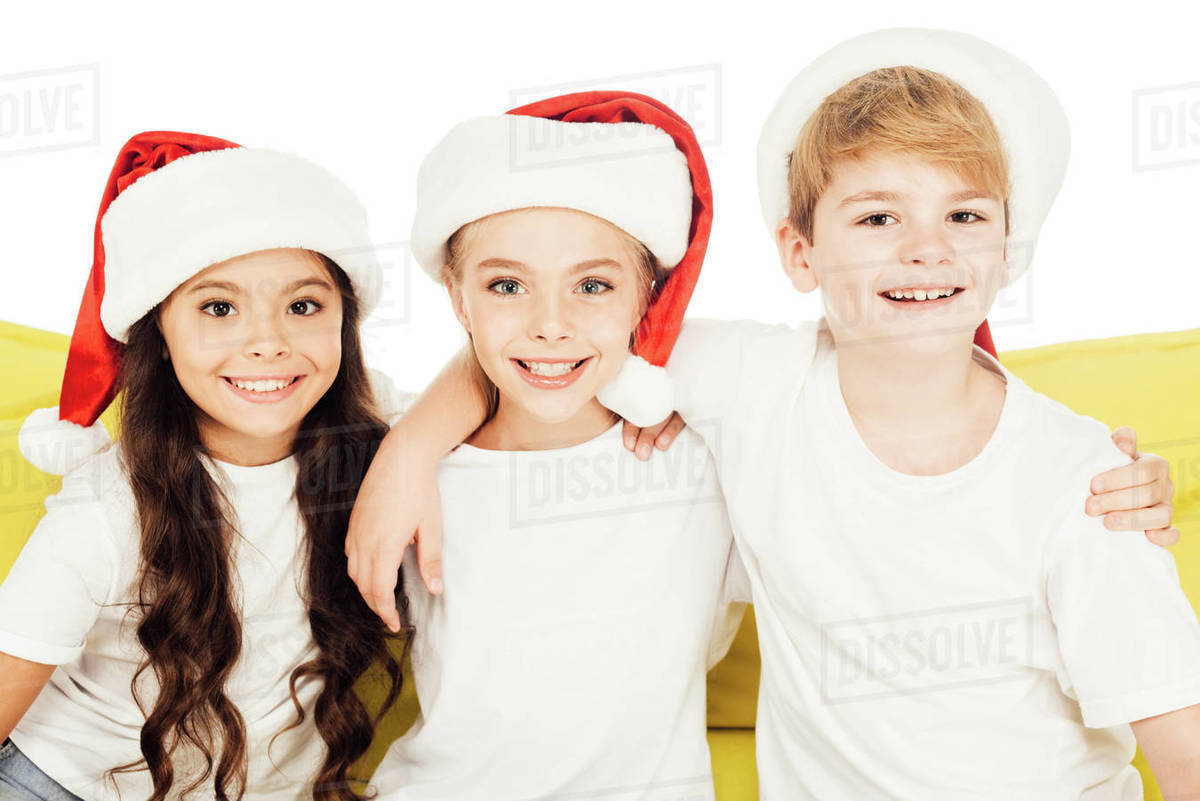 Portrait of smiling adorable kids in Santa hats sitting on yellow sofa ...