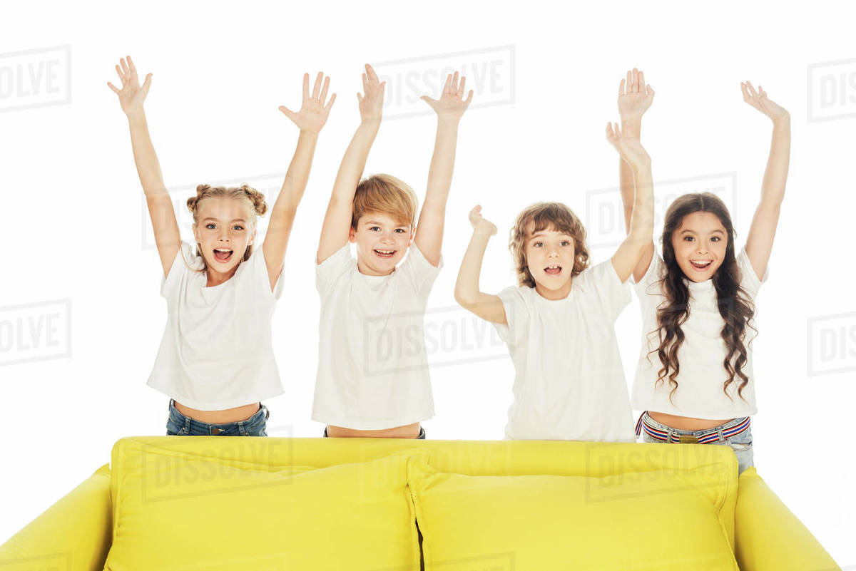 Happy children standing behind yellow sofa with raised hands isolated ...