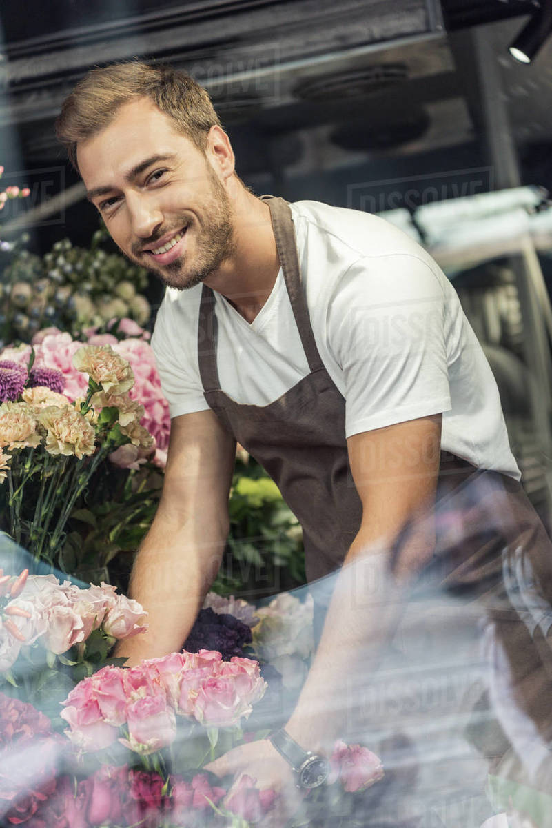View through window of smiling handsome florist taking care of bouquets ...