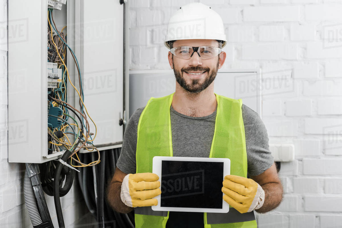 Smiling handsome electrician showing tablet with blank screen near ...
