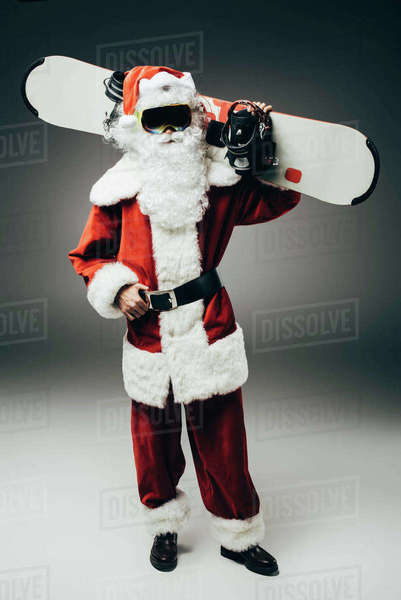 Santa Claus in ski mask holding snowboard over shoulder on grey ...