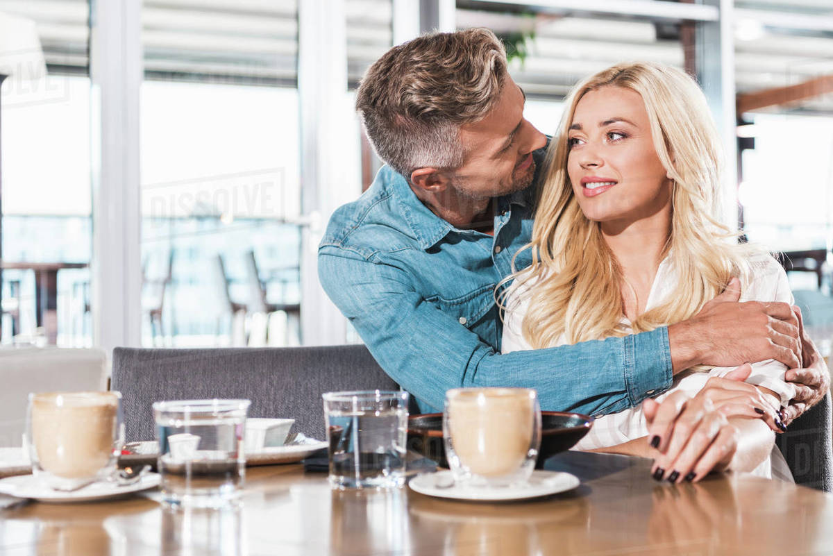 Handsome boyfriend cuddling attractive girlfriend at table in cafe ...