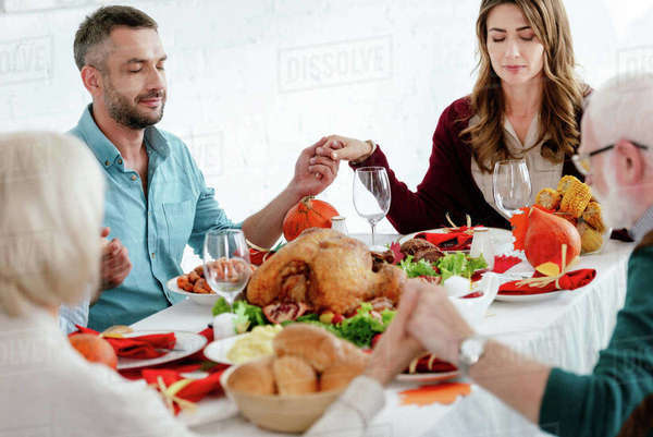 Family praying at served table with turkey before thanksgiving ...