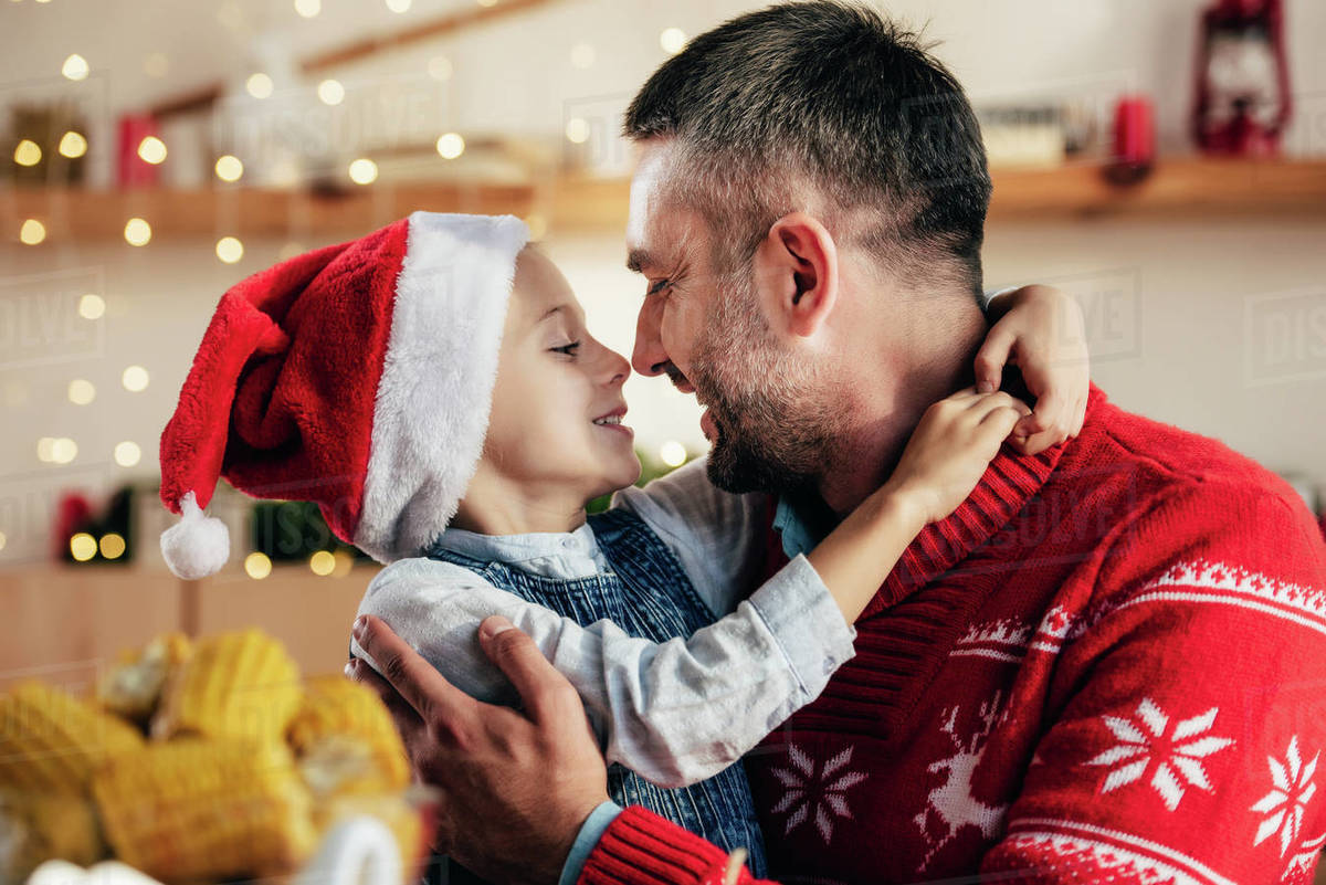 Side view of happy father and little daughter in christmas hat face to ...