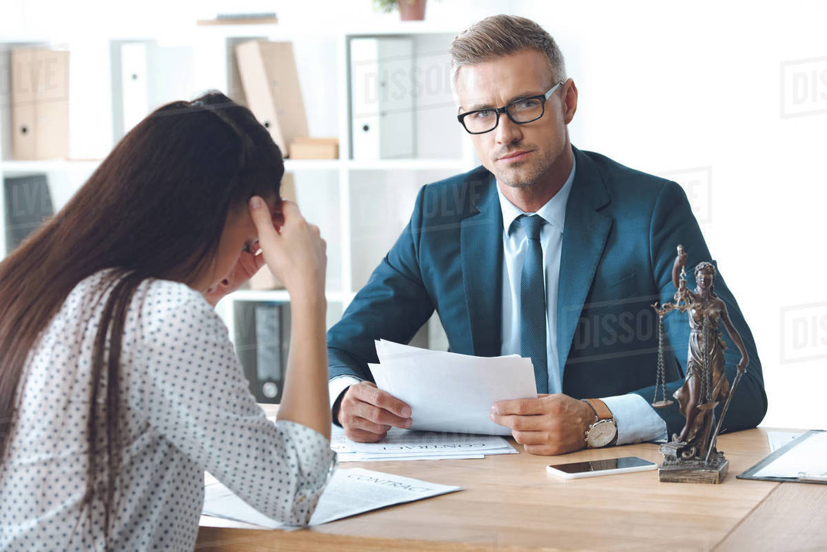 Lawyer holding papers and looking at camera while working with sad ...