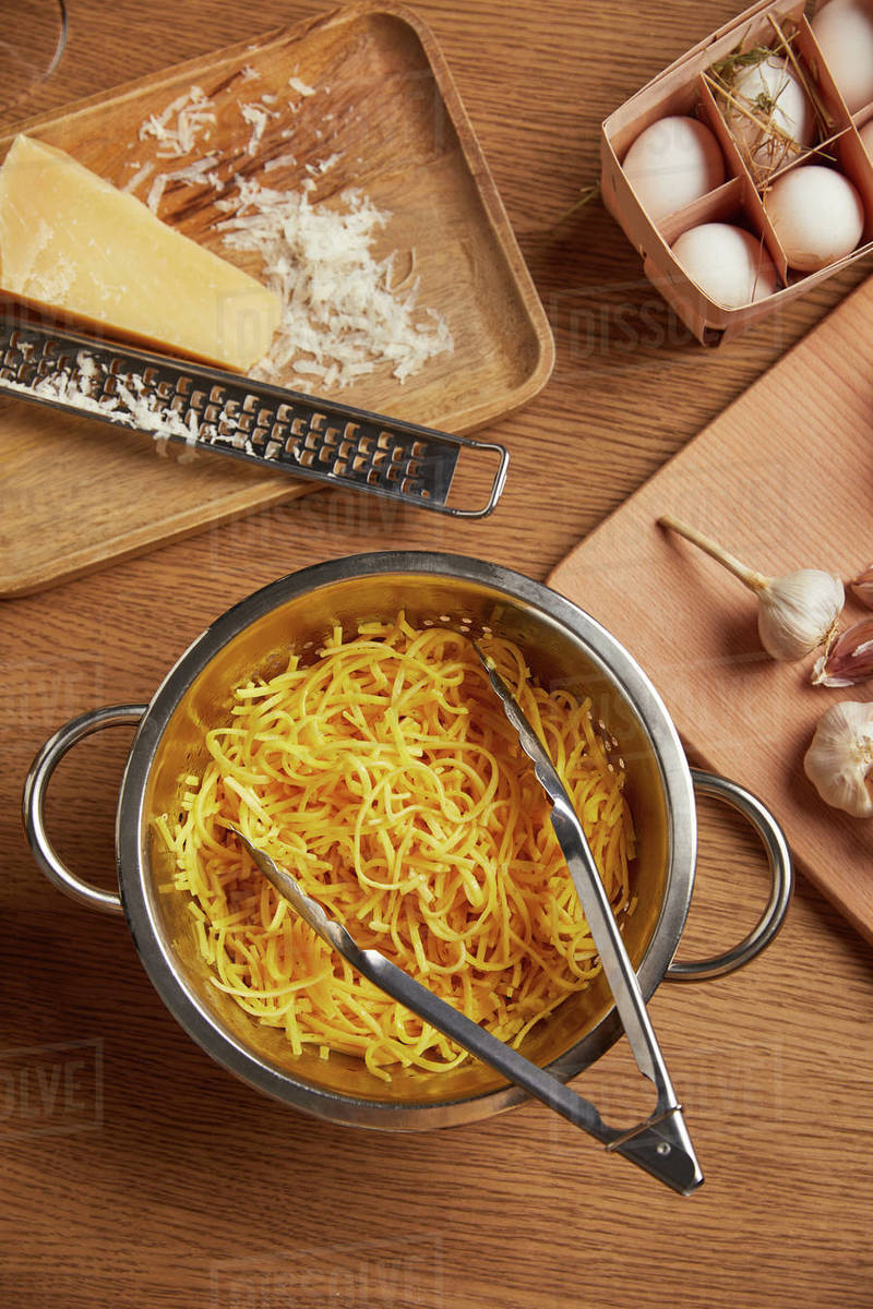 Top view of spaghetti in metal colander surrounded with ingredients for ...