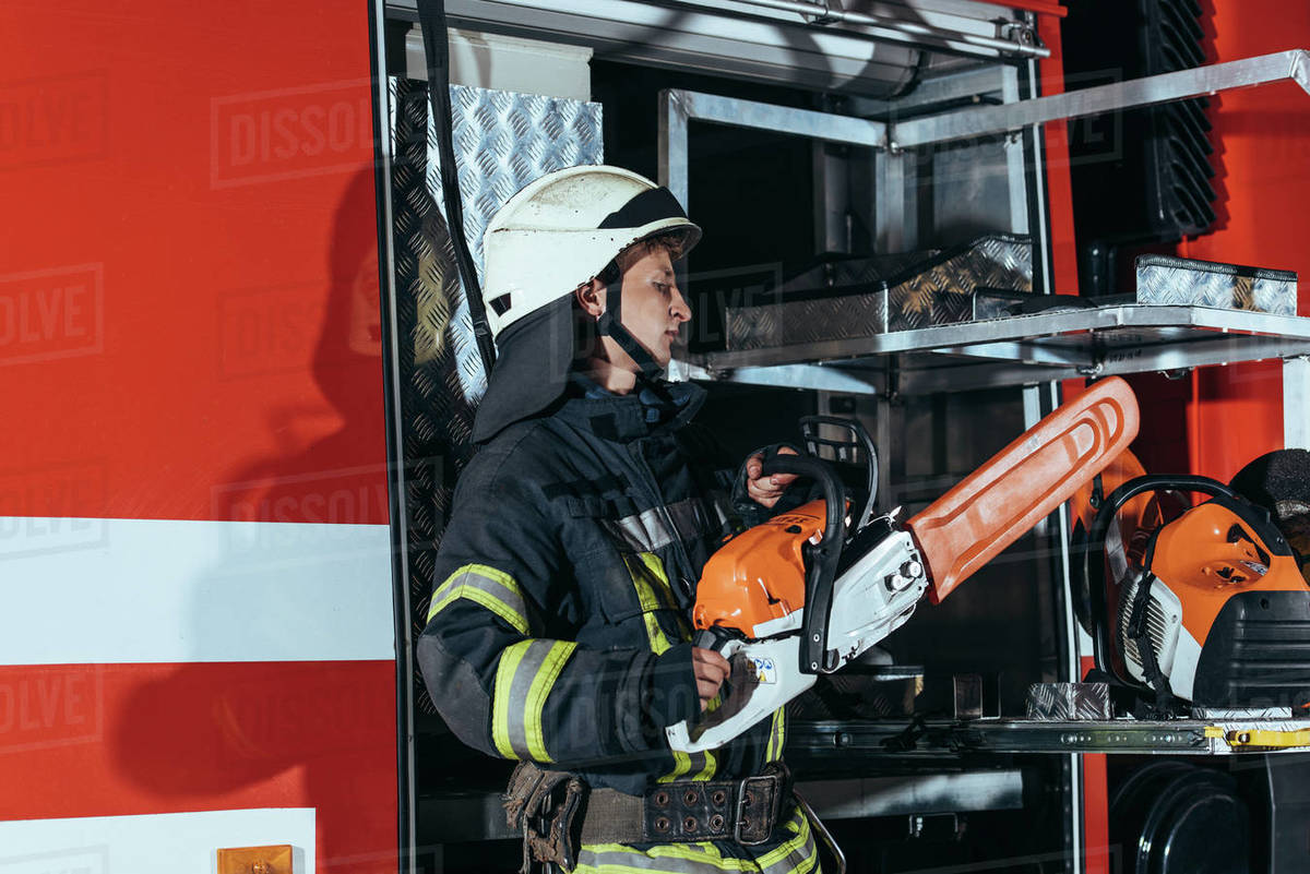 fireman in helmet holding electric saw while standing at truck at fire ...