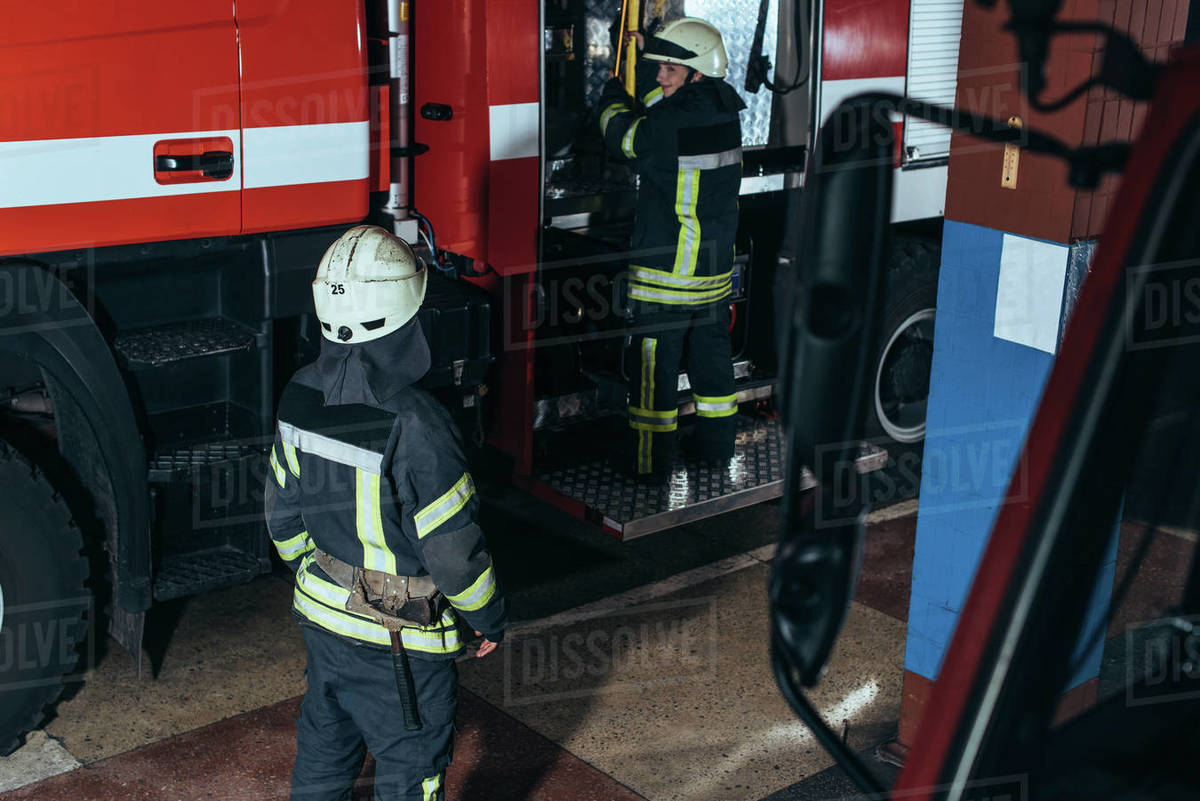 partial view of firefighters in fireproof uniform and helmets at fire ...