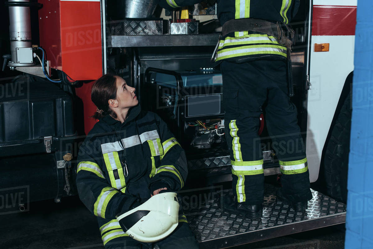 partial view of female firefighter in helmet looking at colleague ...