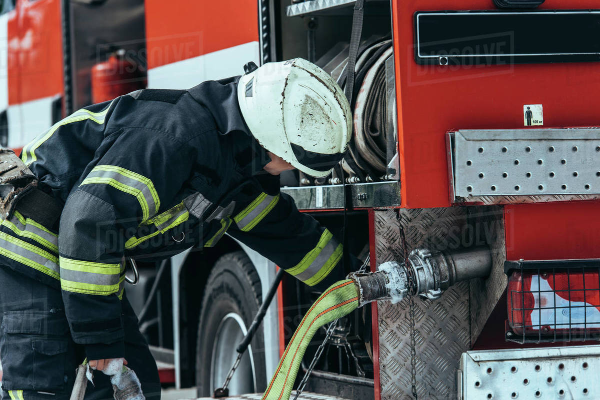 firefighter in protective uniform checking water hose in truck on ...