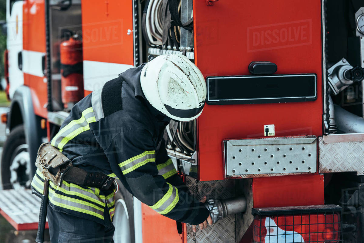 partial view of firefighter in protective uniform checking water hose ...