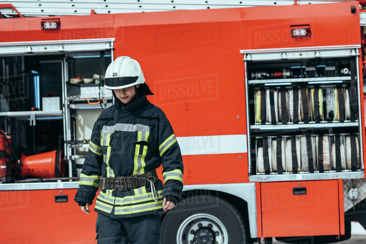 male firefighter in uniform standing on street with red fire truck ...