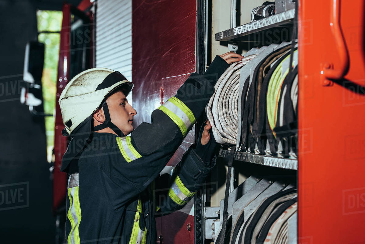 side view of fireman in protective uniform checking equipment in truck ...