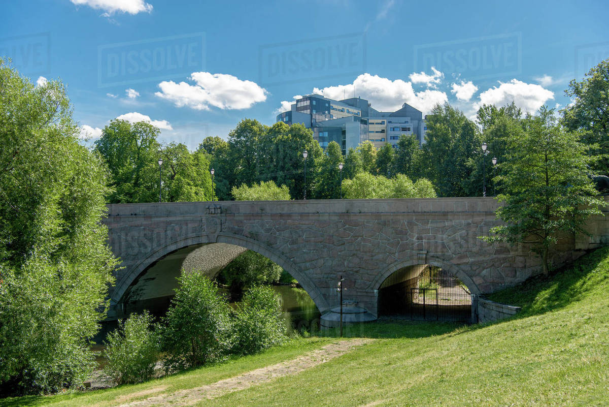 Beautiful old bridge across river, green plants and modern buildings ...