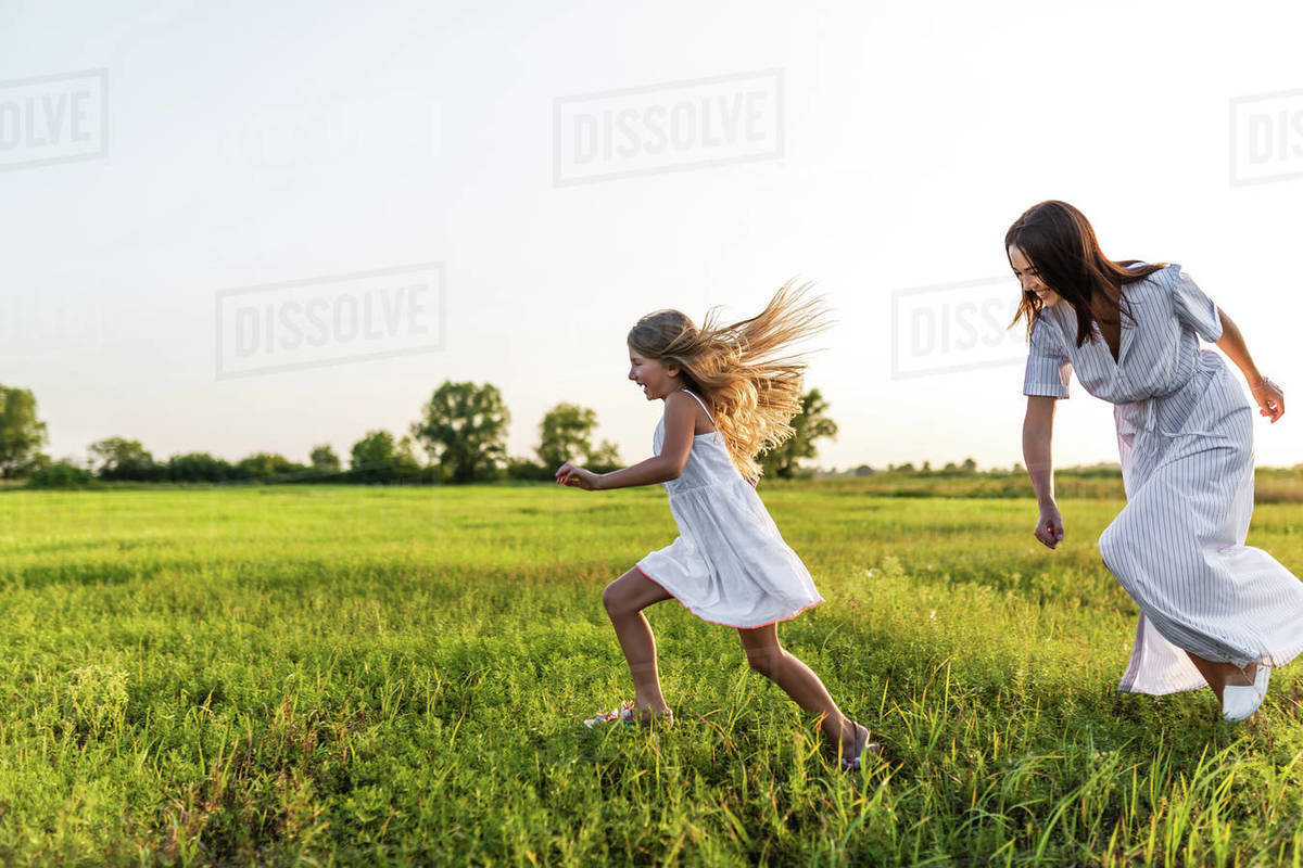 Mother and daughter in white dresses running in green meadow - Royalty ...