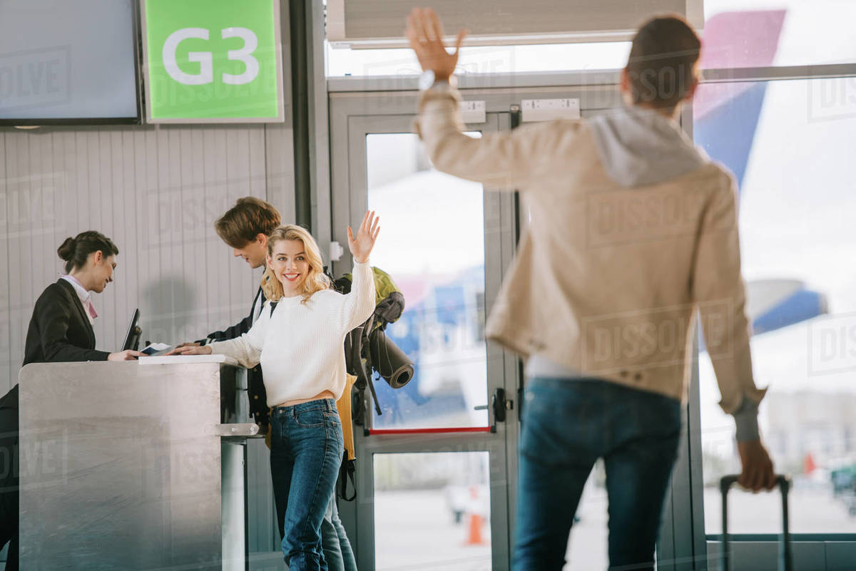 Happy young friends waving hands at check-in desk in airport - Stock ...