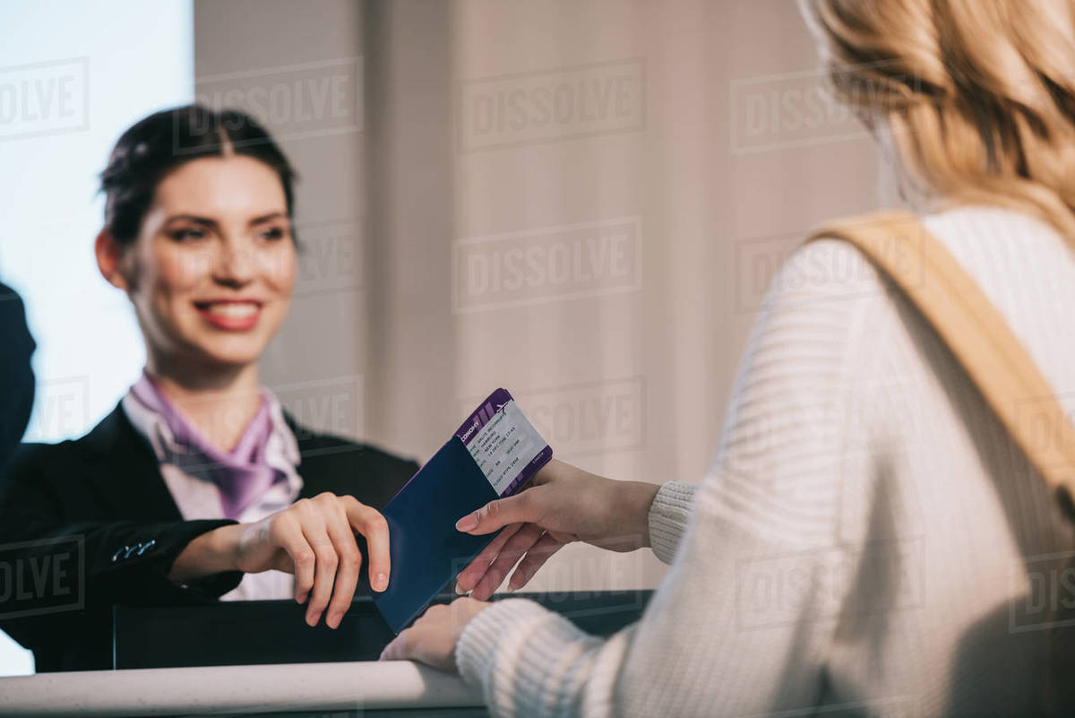 Smiling airport worker giving passport with boarding pass to young ...