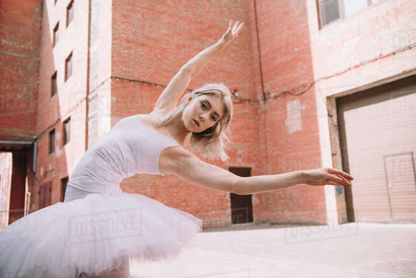 Low angle view of young ballerina looking at camera while dancing on ...