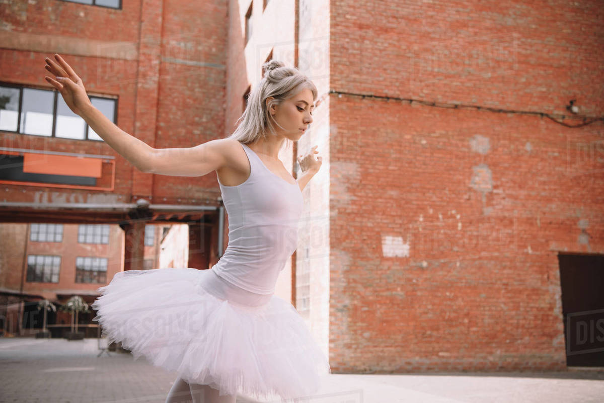 Attractive young ballerina in white tutu dancing on street - Stock ...