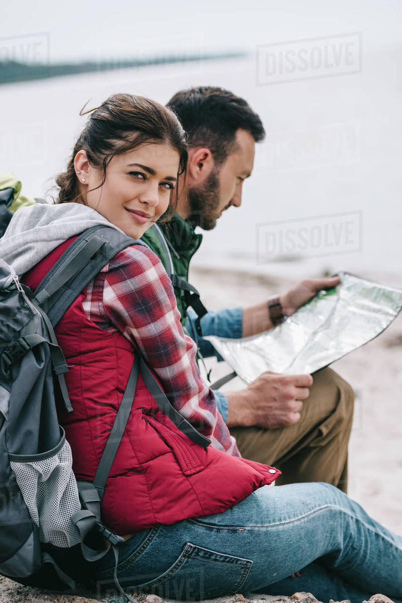 Side view of hikers with map sitting on rocks on sandy beach - Royalty ...