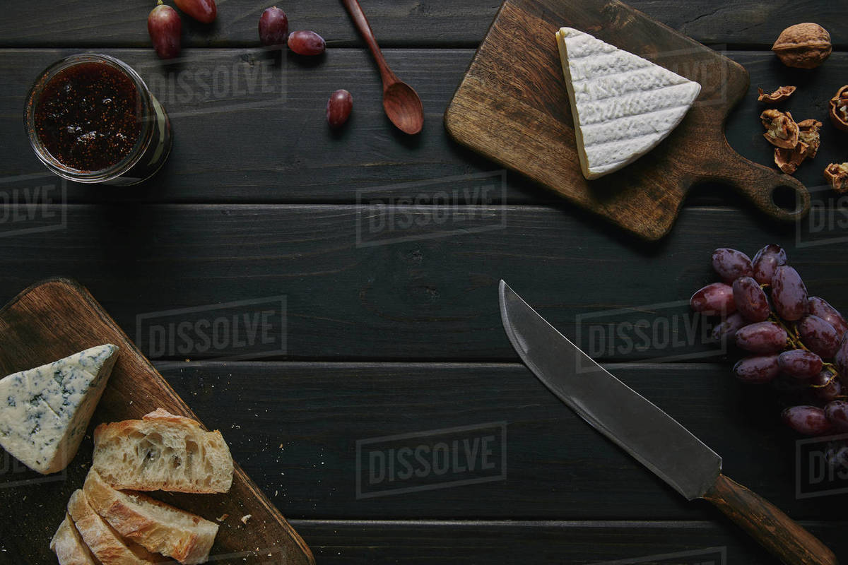 Top view of knife, delicious jam and gourmet snacks on wooden table ...