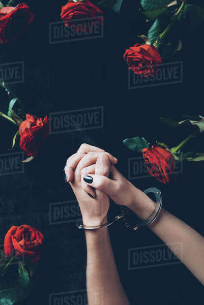Cropped shot of woman in handcuffs above black fabric with red roses ...