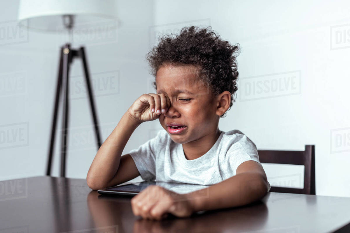 Little African American boy crying while sitting with digital tablet ...