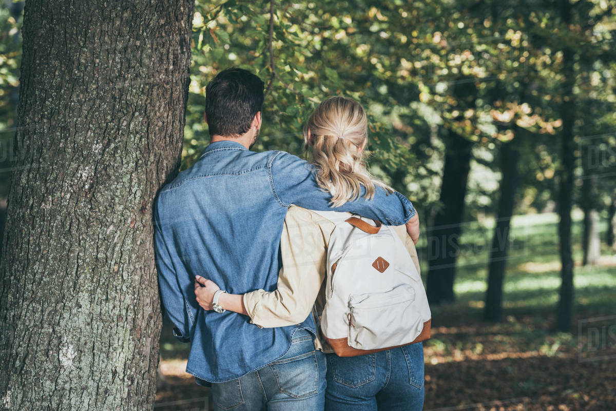 Back view of stylish couple hugging near tree in park - Stock Photo ...